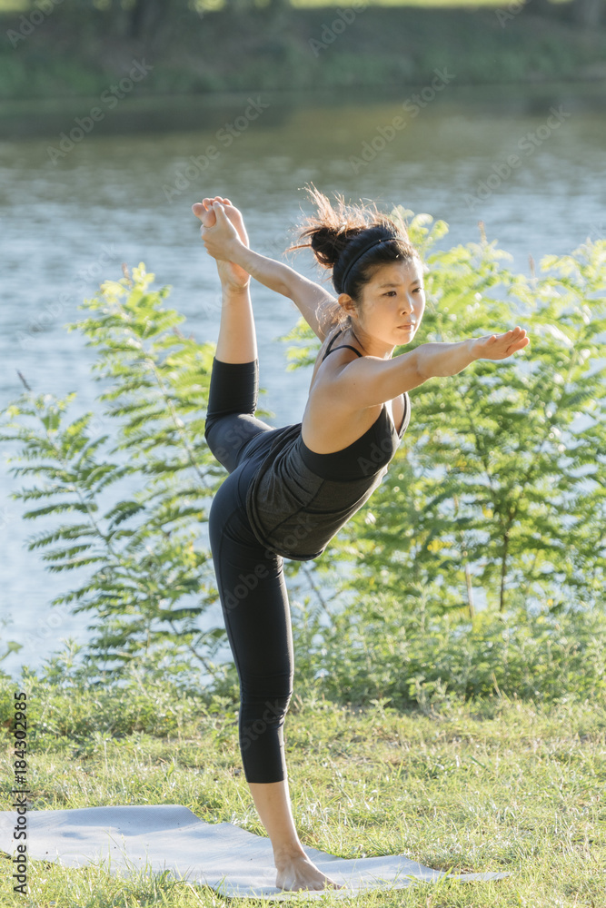 Young Japanese woman practicing yoga exercises near a river in a summer ...
