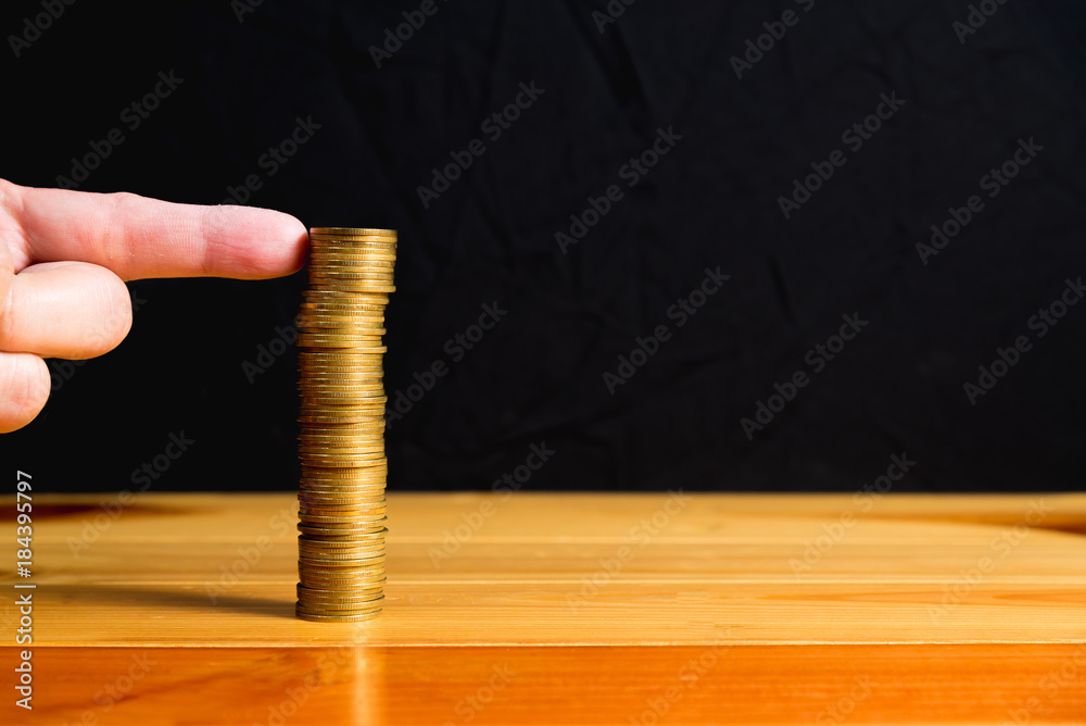 Finger pushing a column of coins on wooden table with black wall, gold ...
