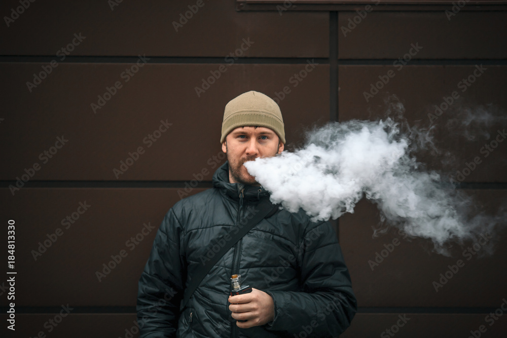 Vape man. Portrait of a handsome young white guy in a modern cap vaping ...