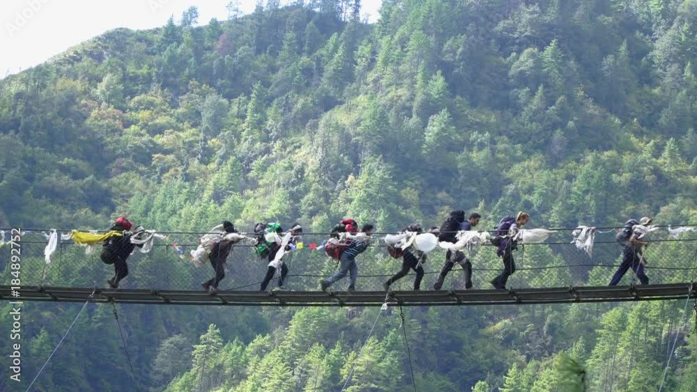 Sherpas and hikers walk a bridge crossing a valley in the foothills of ...