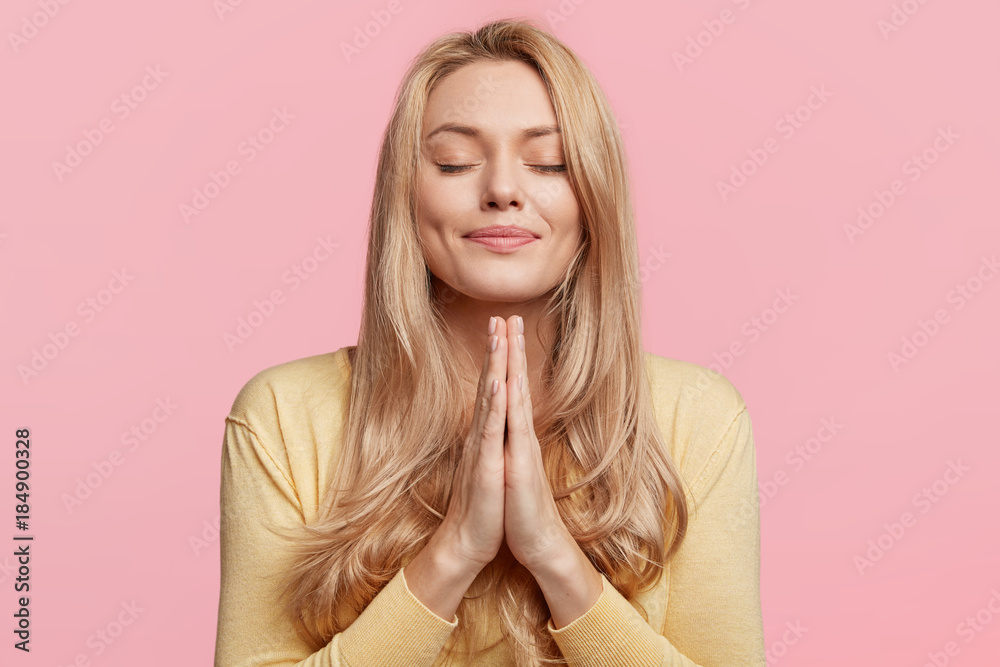 Photo of hopeful blonde female keeps hands together in praying gesture ...