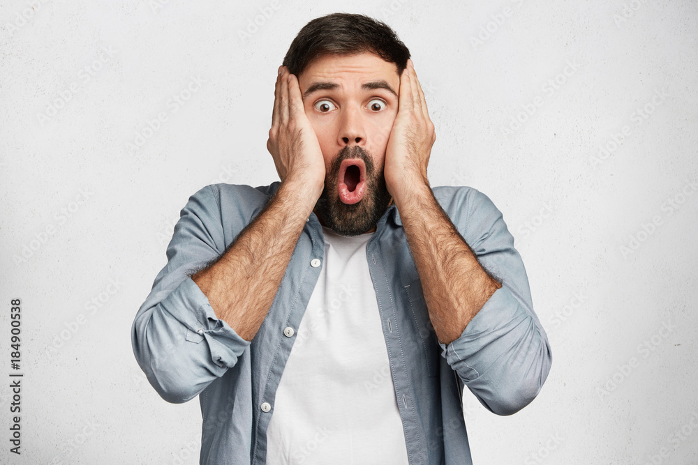 Horrified bearded male looks in terror at camera, keeps mouth widely ...
