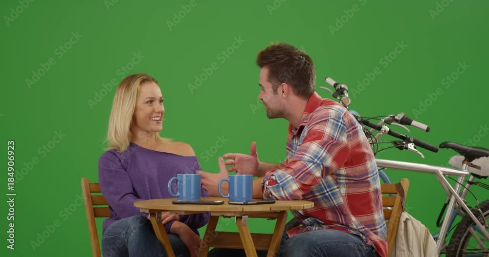 Cute young modern couple sitting outside a coffee shop talking on green ...