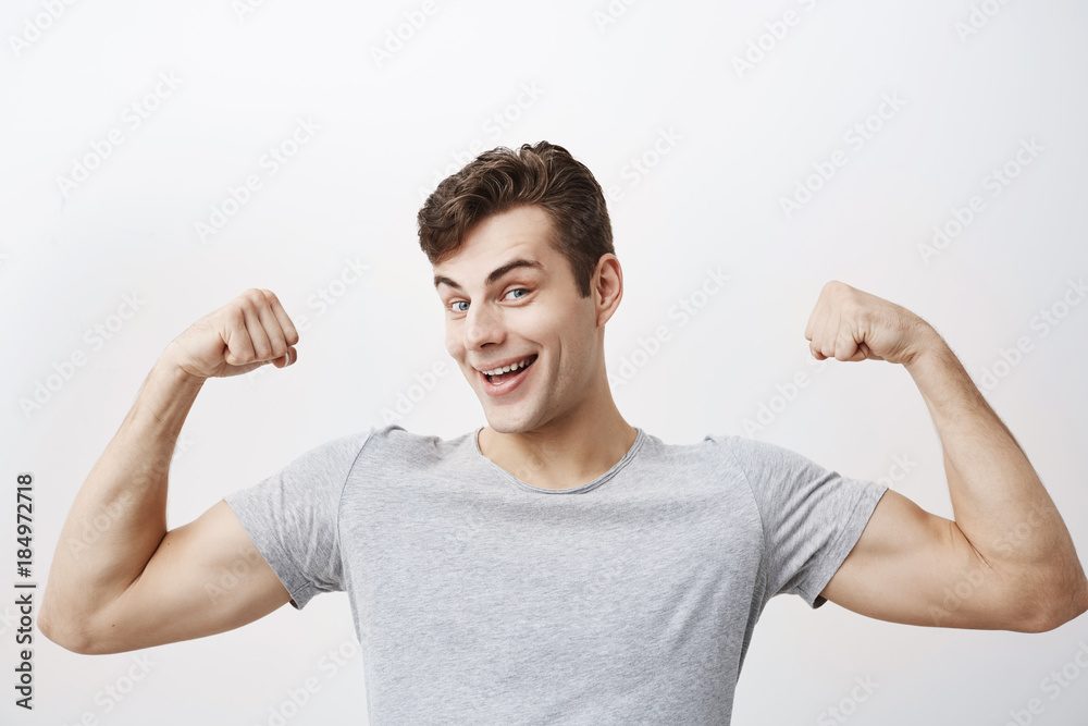 Positive emotional man smiles, shows muscles on his arms, feels proud ...