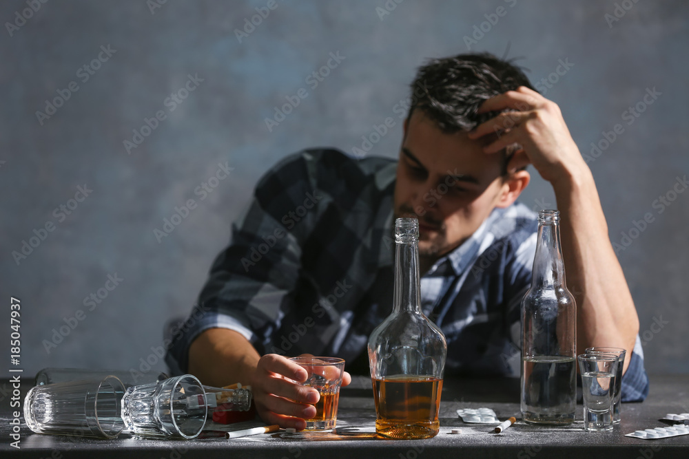 Drunk man sitting at table with alcohol and drugs. Alcoholism concept ...