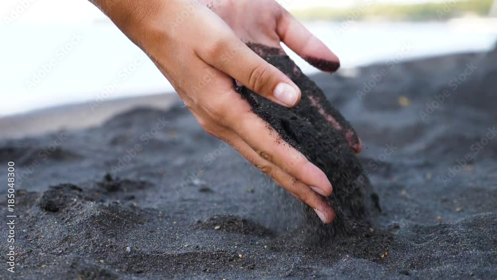 Female hand is poured by black volcanic sand through fingers on the ...