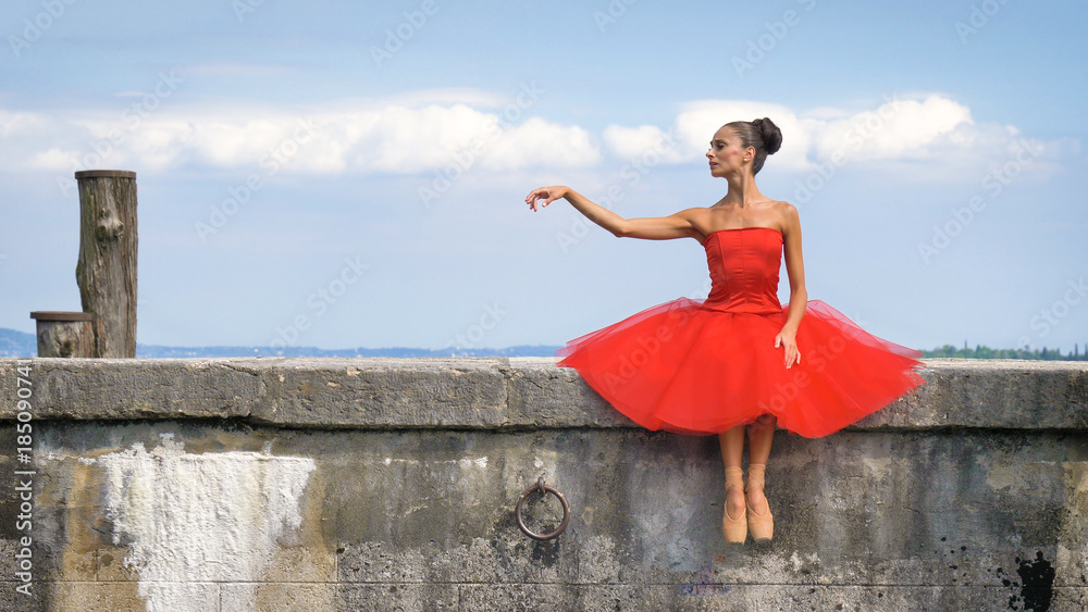 Portrait of a beautiful light ballerina, in a lush red dress, sits on a ...