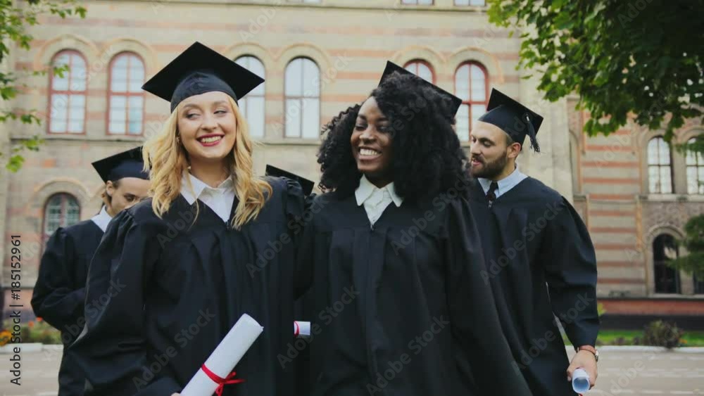 Happy smiled mixed races graduates walking with the diplomas in hands ...
