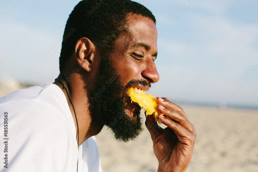 Man with beard and dark skin eating mango on sea shore Stock Photo ...