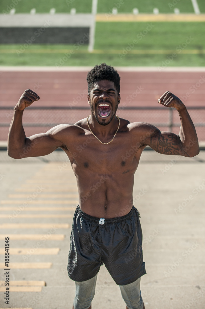 Muscular Jamaican athlete performing double bicep pose with primal ...