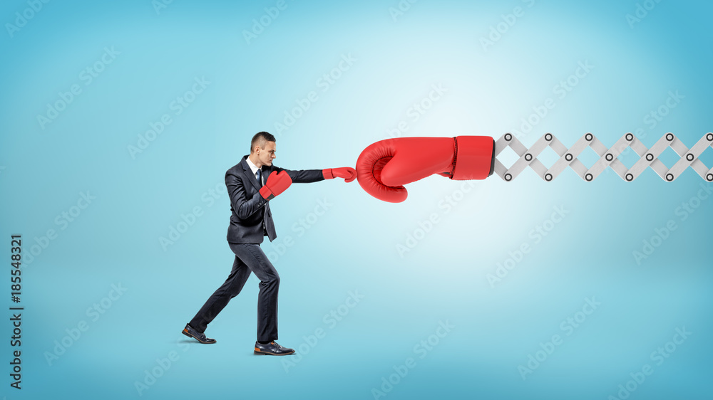 A small businessman in sport gloves punches a giant red boxing glove on ...
