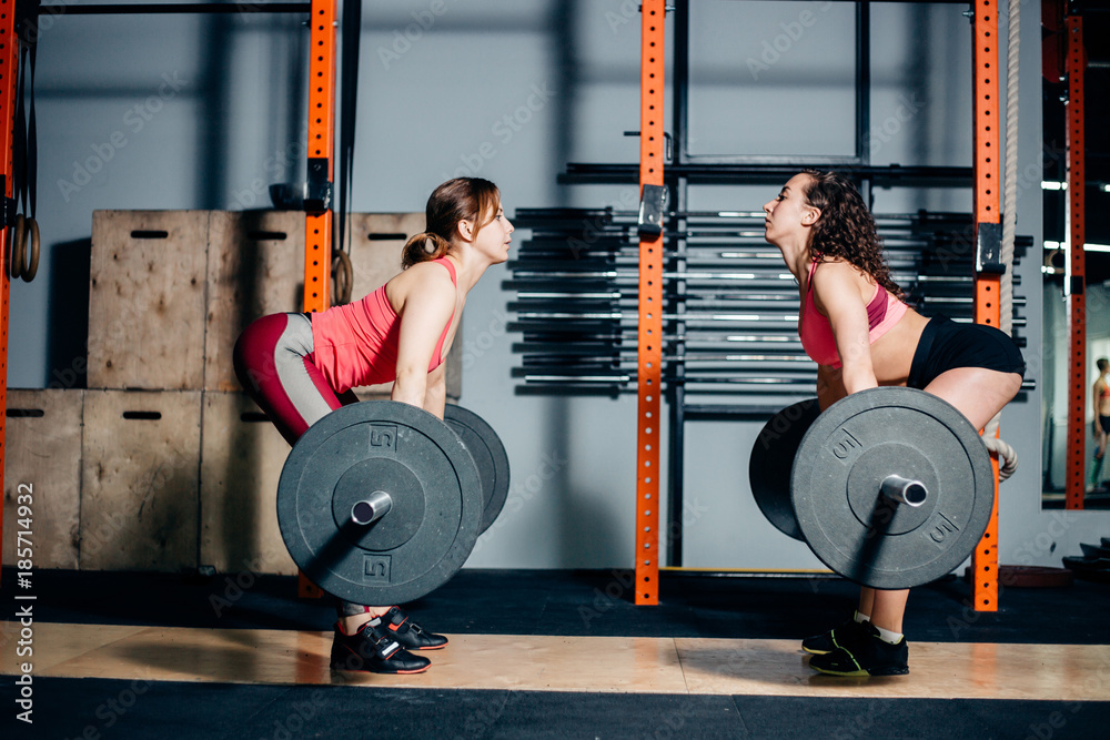 Sportive athletic womans lifting heavy barbells in light spacious gym ...
