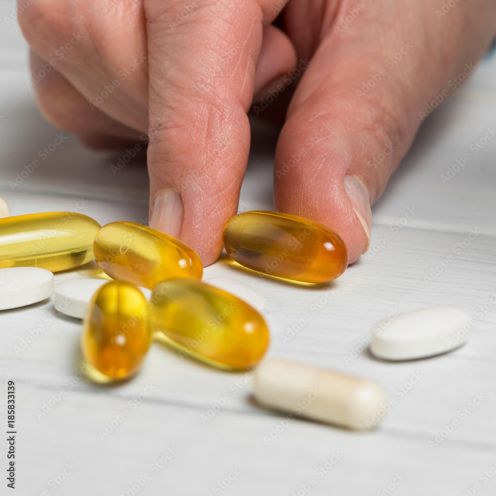 Woman hands takes yellow capsules of omega 3, white pills of calcium ...
