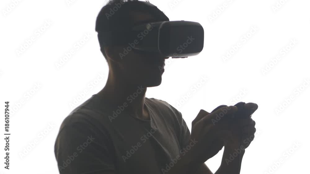 Silhouette of young man playing game in vr glasses. Guy gets experience ...