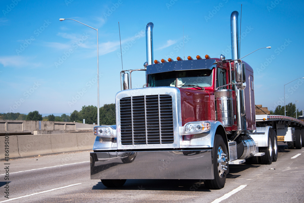 Classic big rig semi truck in dark red and flat bed semi trailer going ...