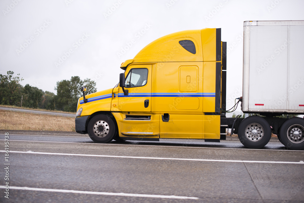 Profile of yellow big rig semi truck with semi trailer running on the ...