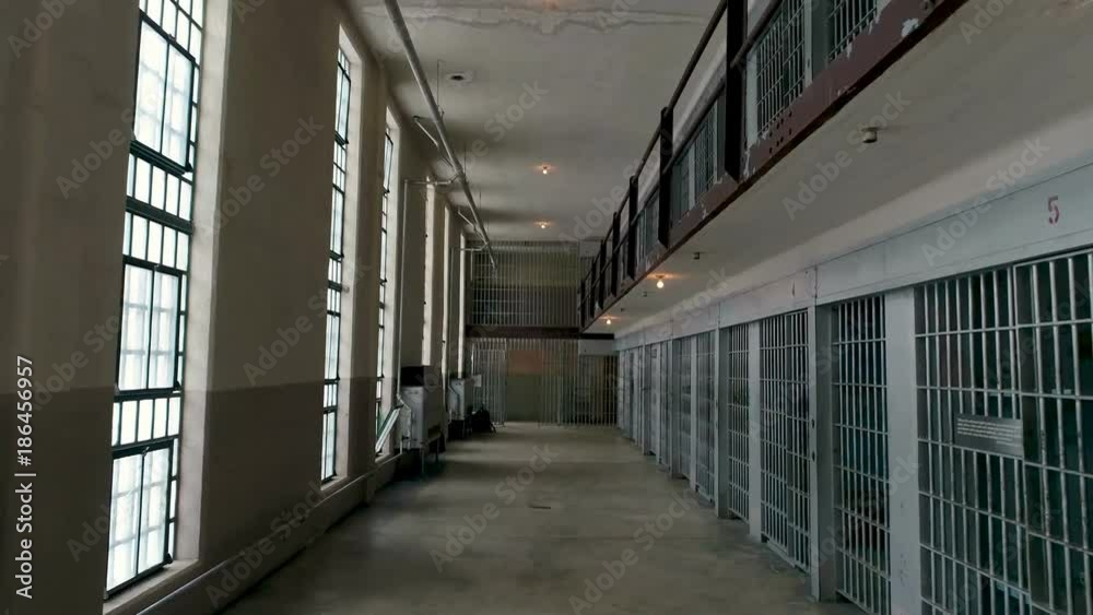 Hallway with prison cells on one side and windows to the outside on the ...