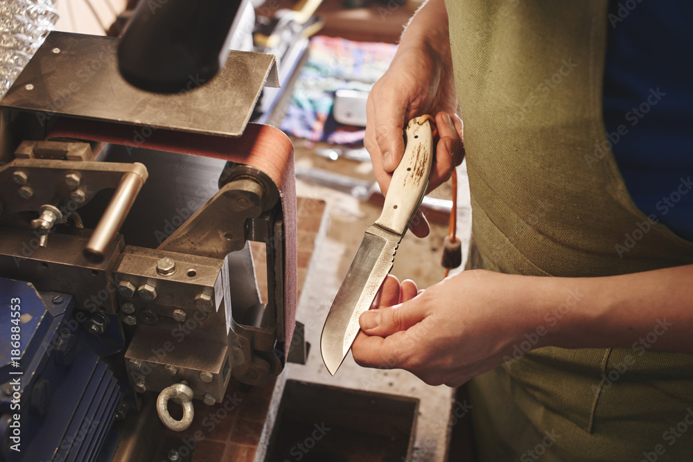 Making of a knife. Master sharpens a blade on the machine closeup in ...