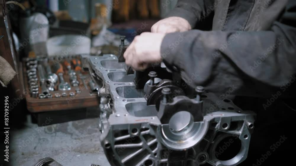 worker is disassembling car engine in a repair shop, twisting bolts and ...
