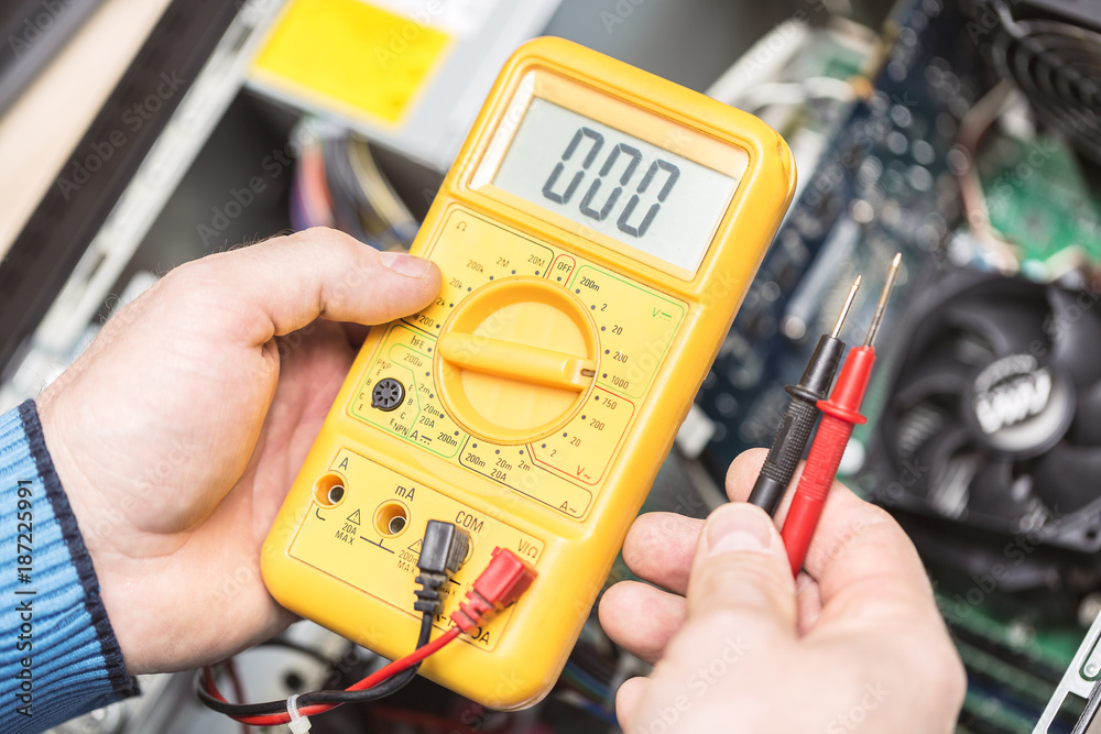Technician hands holding voltmeter above computer motherboard. Repair ...