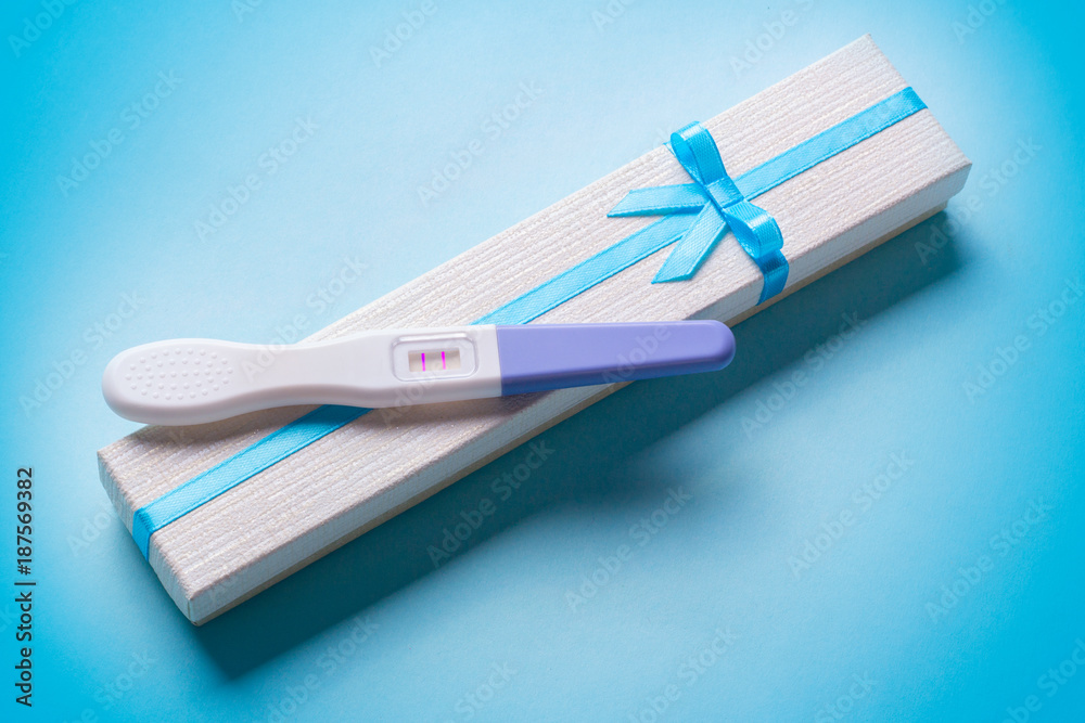 Positive pregnancy test with two strips and a gift box with a blue ...