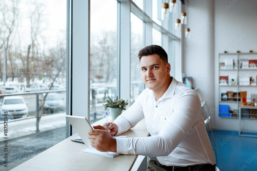Young handsome businessman posing with tablet at office at a window ...