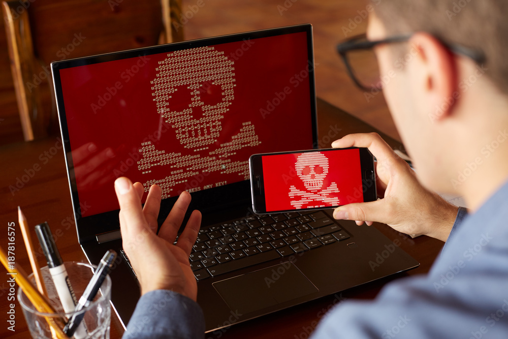 Man sits near laptop with phone blocked and encrypted by ransomware ...