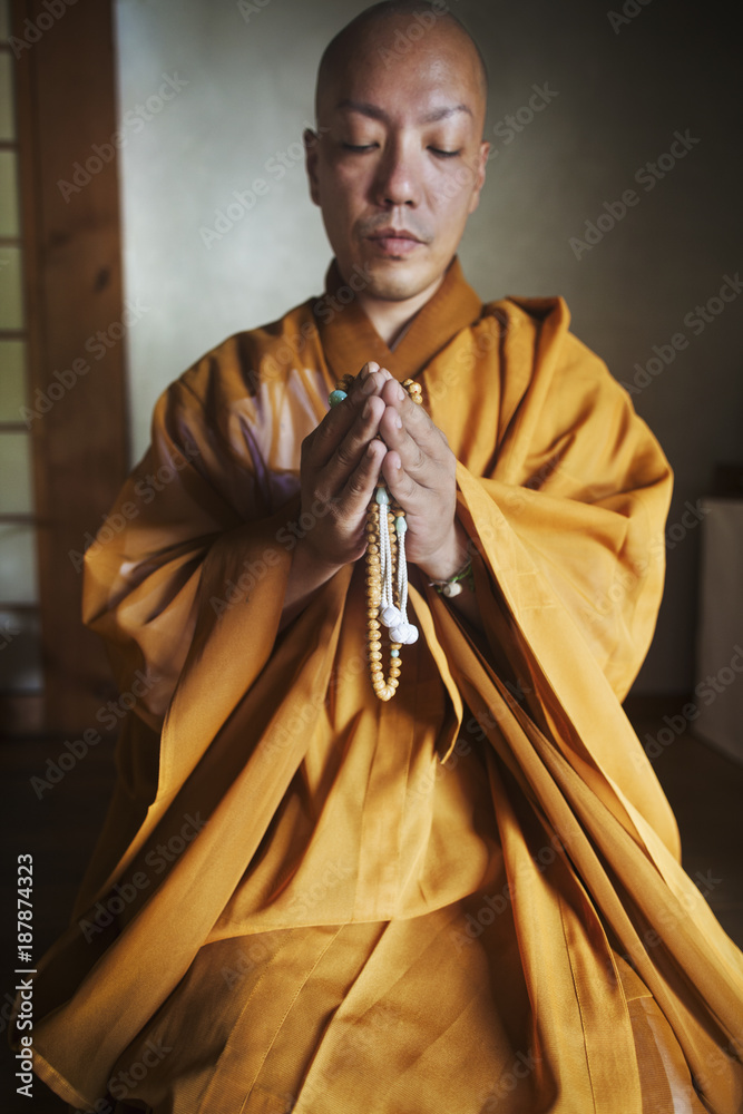 Buddhist monk with shaved head wearing golden robe kneeling indoors in ...