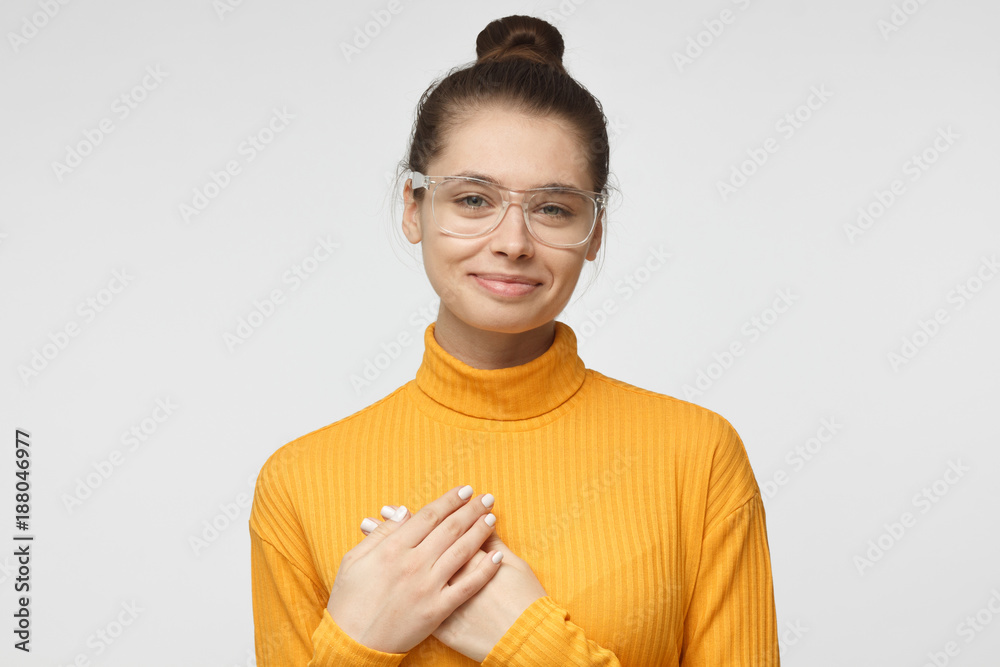 Portrait of smiling positive young female keeps hands on chest ...