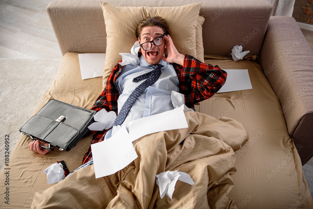 Scared guy lying in bed and screaming. He is looking at camera with ...