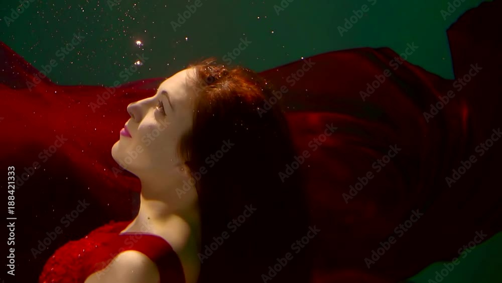 sinking girl with long red hair is under water in a dark pool with ...