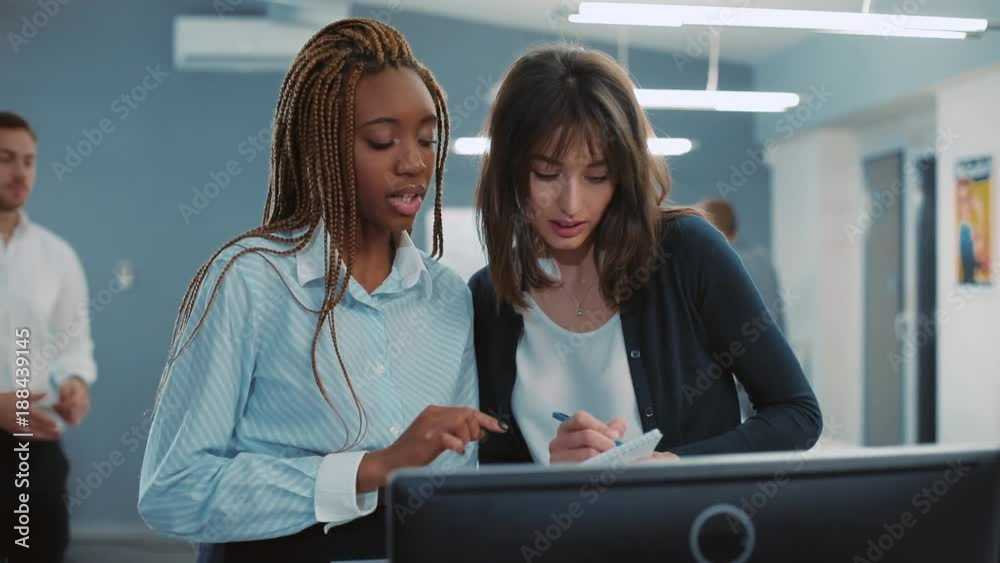 Two attractive girls standing near computer in beautiful office ...