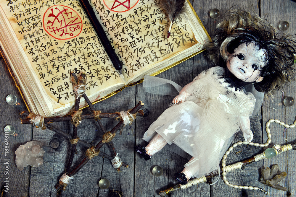 Scary doll, pentagram and open magic book with evil symbols on witch ...