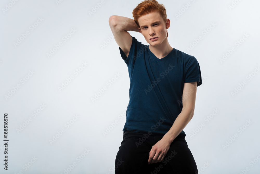 Sporty. Attractive humourless red-headed young man sitting on the chair ...