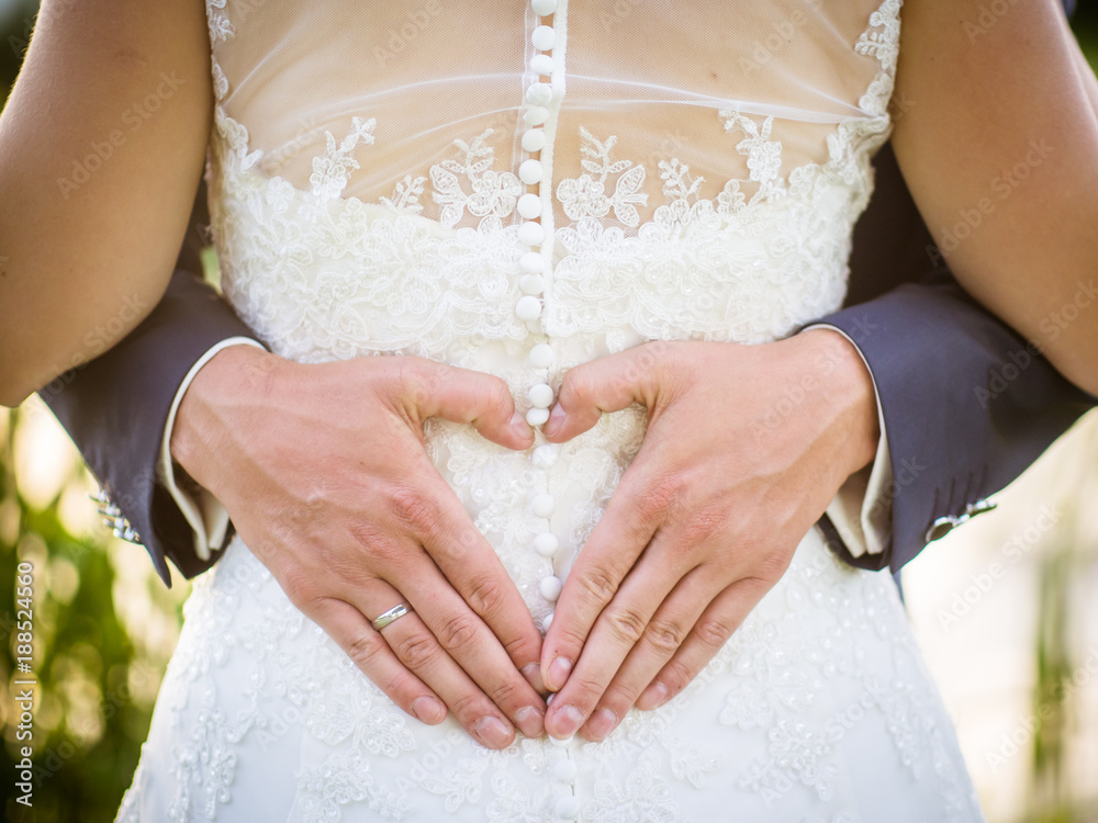 Groom creating heart shape with his hands on the back of the bride ...