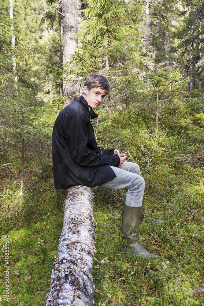 Teenage boy sitting on fallen tree in forest Stock Photo | Adobe Stock