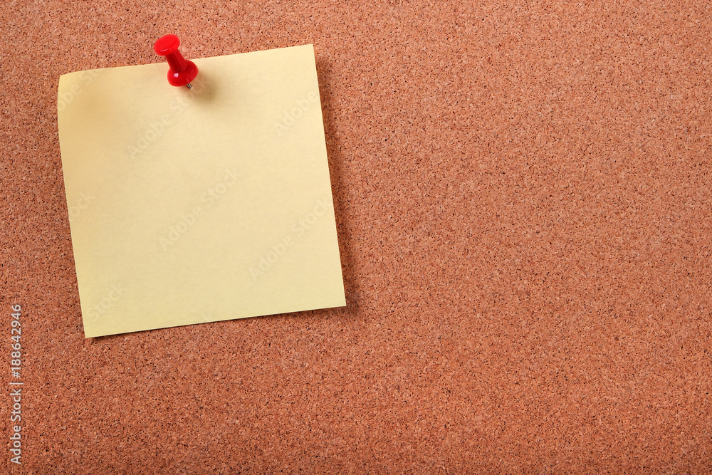 One single yellow square sticky post it note pinned with pushpin to a ...