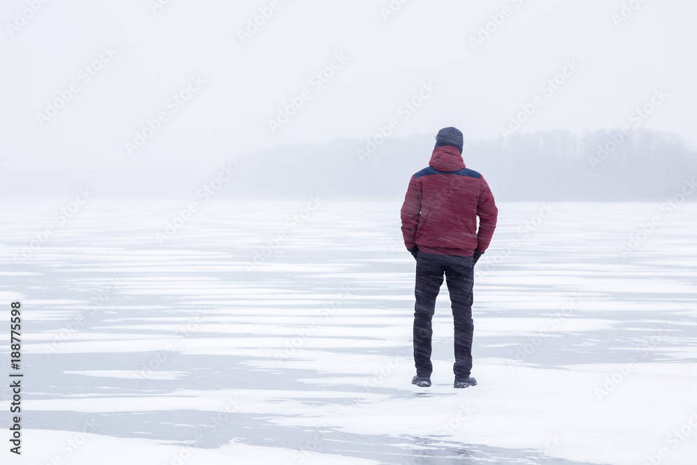 Young man in snow blizzard standing alone on the lake ice and staring ...