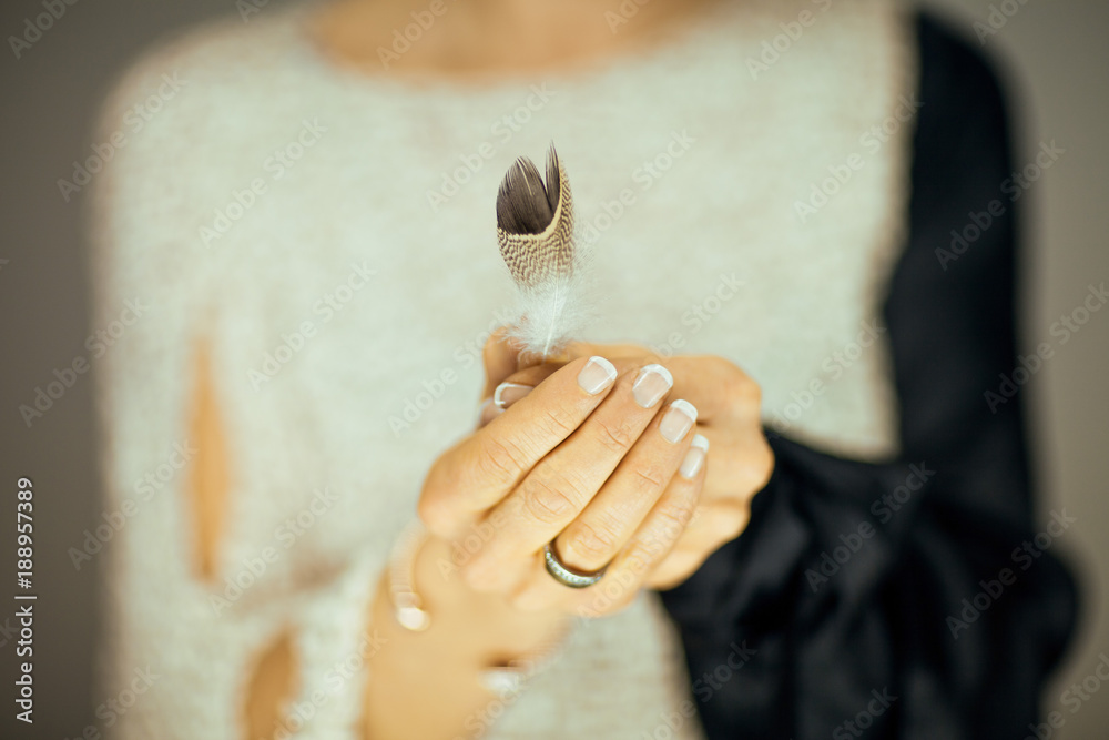 woman hands holding single feather in her hands, light pastel colors ...