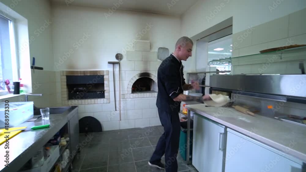 A young pizza maker prepares pizza in the kitchen of the restaurant ...