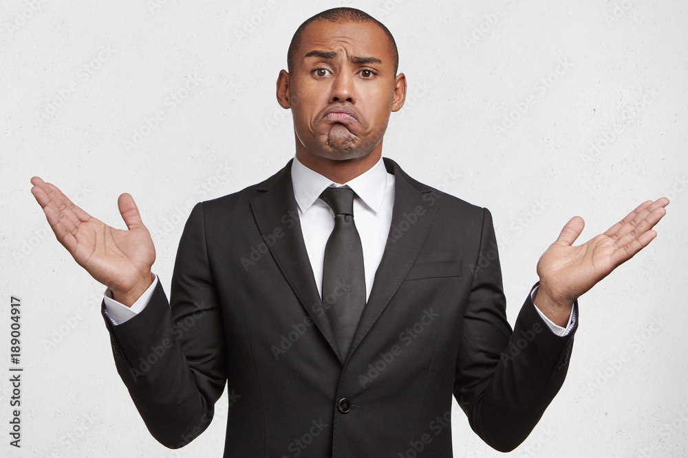 Isolated shot of hesitant dark skinned male curves lips and shrugs ...