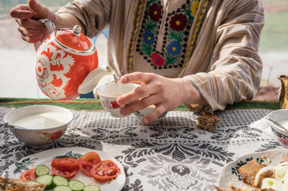 Young man in traditional clothing of Tajikistan pouring tea in ...