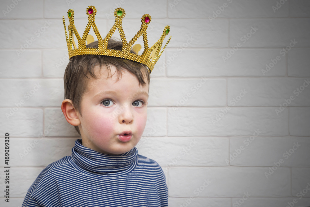 Child with a golden crown on his head against a brick wall background ...