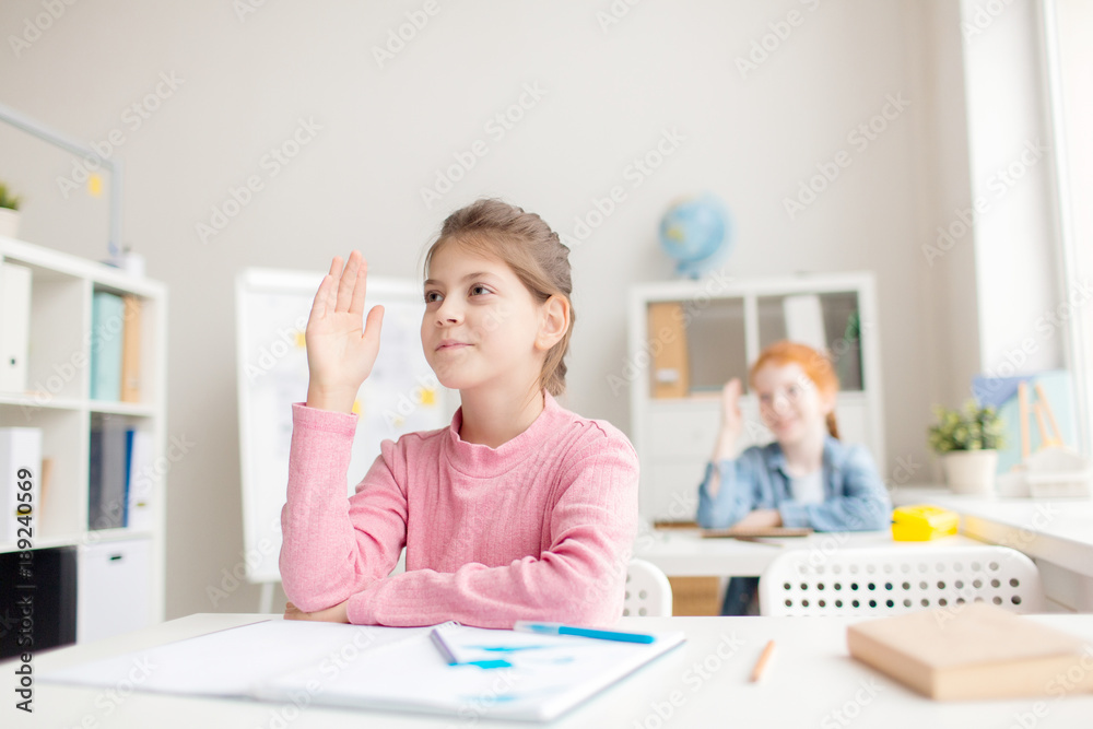 Diligent pupil by desk raising hand at lesson to answer question of ...