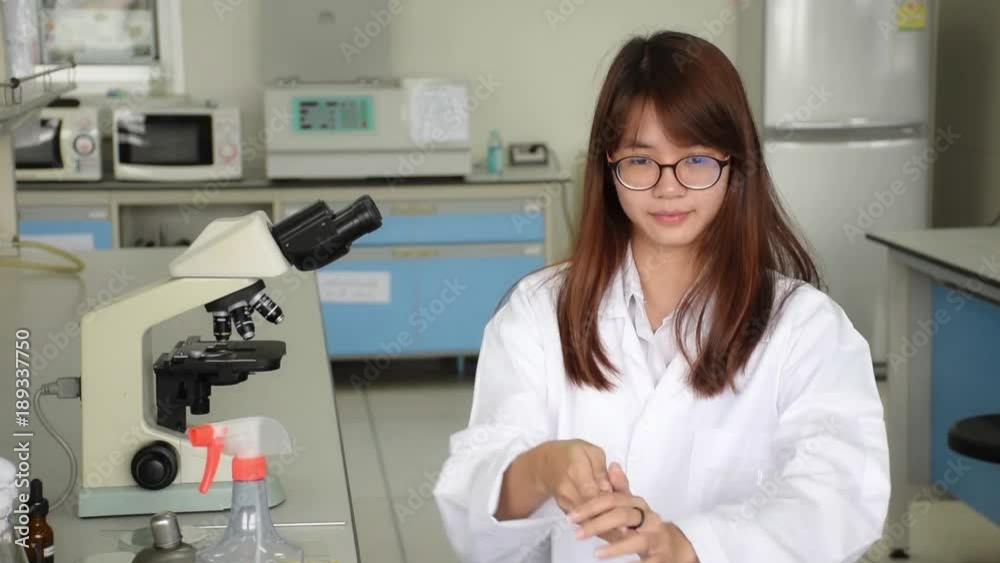 Asian Thai female scientist or science college student spraying hands with alcohol before ...