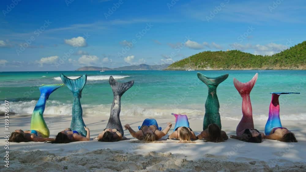 group of mermaids raising their tails in sync on tropical beach in the ...