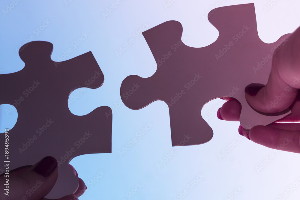 two hands trying to connect couple puzzle piece on sky background. one ...