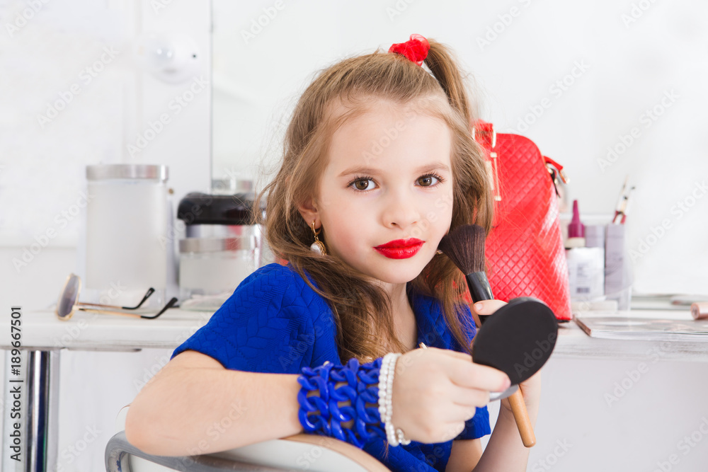 beautiful little girl in the mirror preening and using makeup to ...