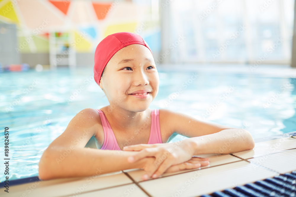 Happy Asian girl in swimwear standing in water of swimming pool during ...