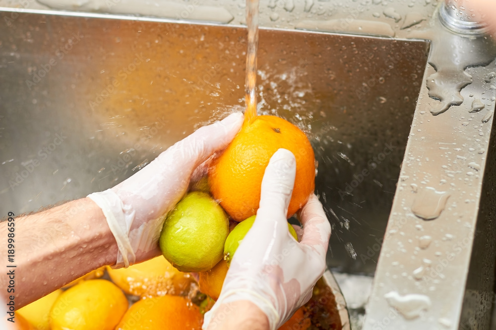 Chef washing citrus fruits in a sink. Tap water flowing on a orange and ...